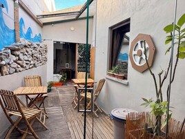 Um deck de madeira com uma mesa e cadeiras, um muro de pedra e uma janela com uma roda decorativa.