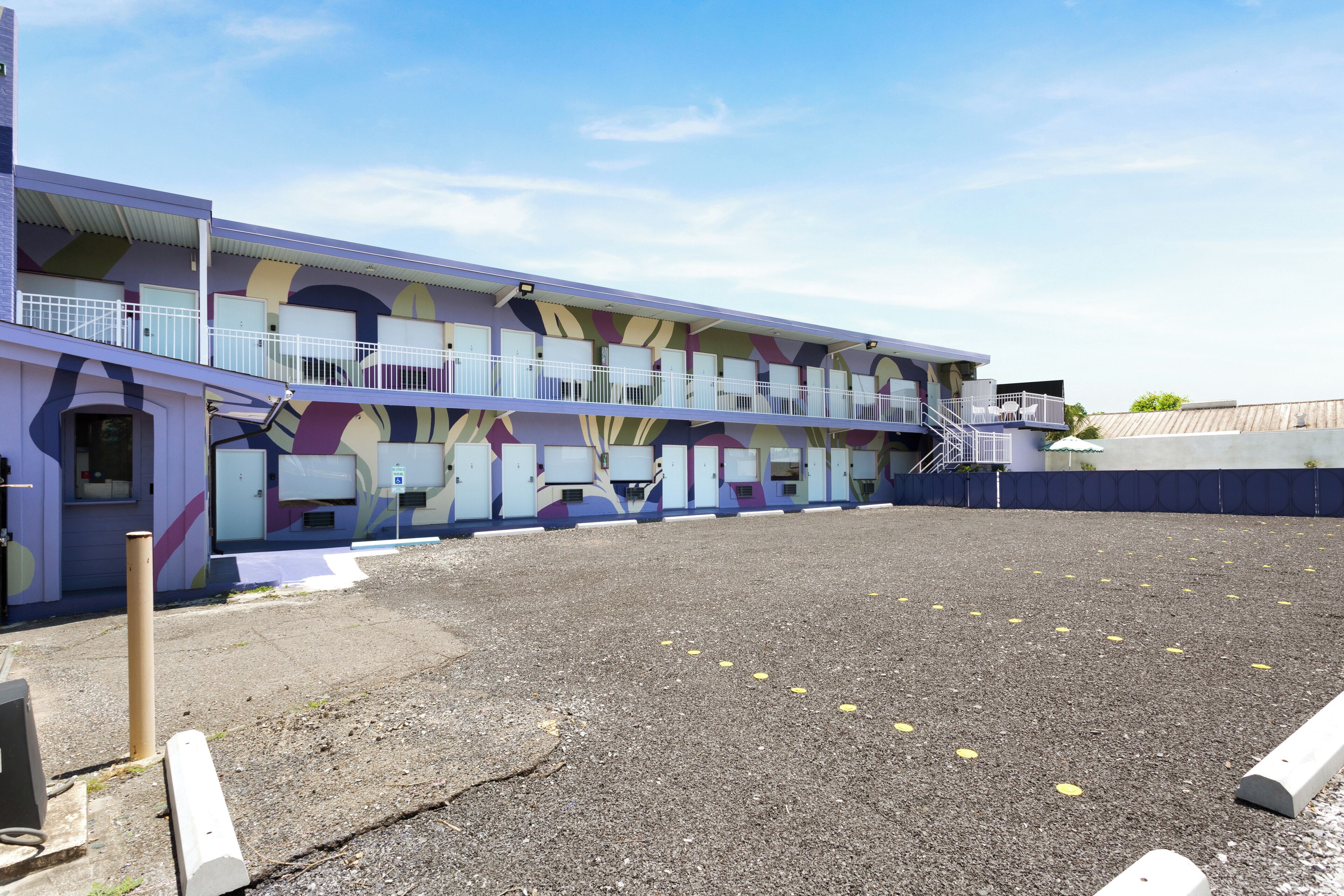 Um motel com estrutura em dois andares, várias varandas e estacionamento com marcações amarelas.