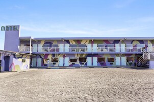Um motel com estrutura em dois andares, vários quartos e uma área externa coberta.