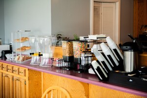 Uma bancada de cozinha com diversos eletrodomésticos e recipientes, incluindo uma cafeteira, um liquidificador e embalagens com alimentos.