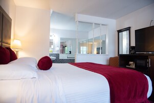 Quarto de hotel com uma cama grande, televisão, espelho e vista para o banheiro.