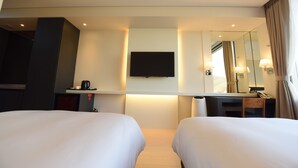 Quarto de hotel com duas camas, uma escrivaninha, televisão e um espelho grande.