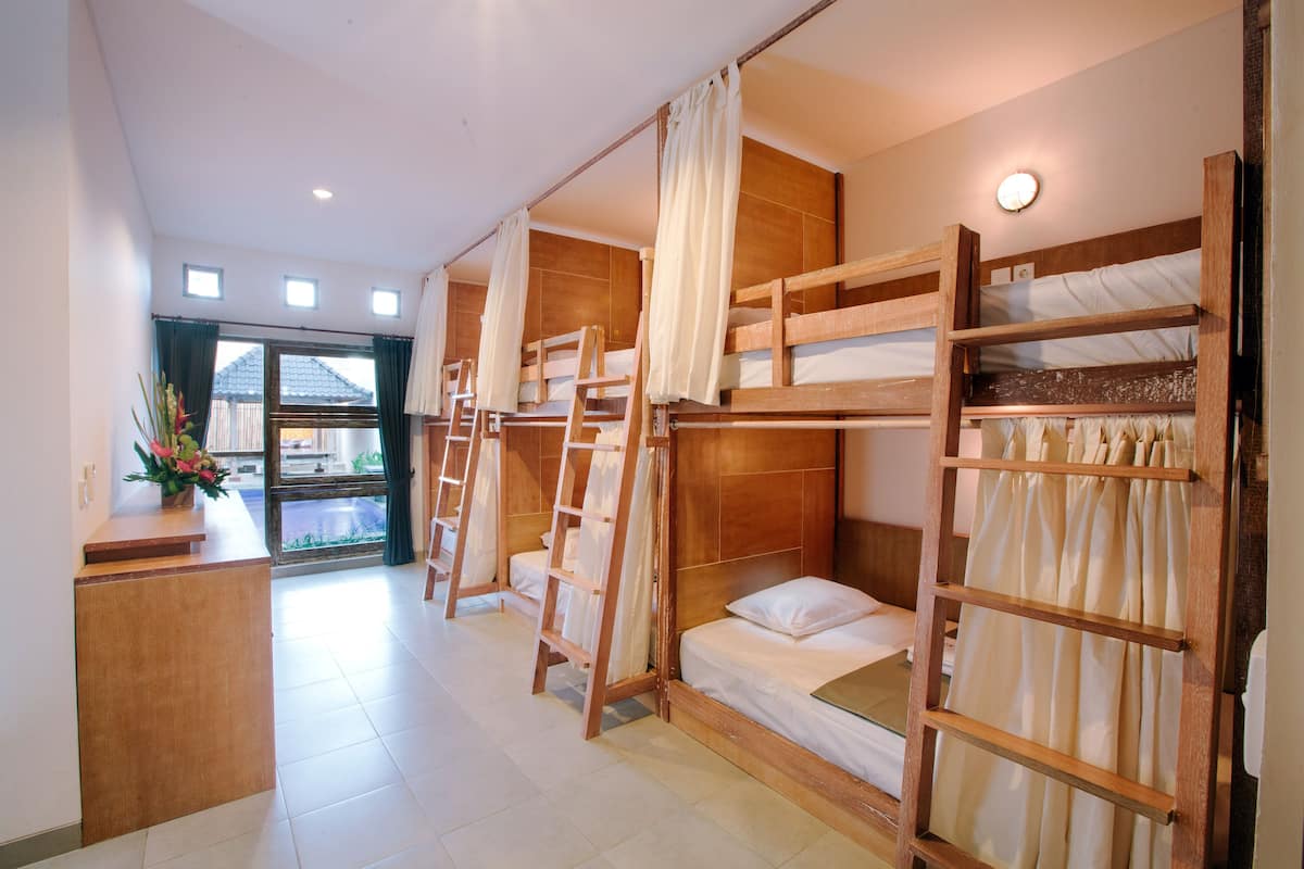 Um dormitório com beliches, uma escrivaninha e uma janela com cortinas.
