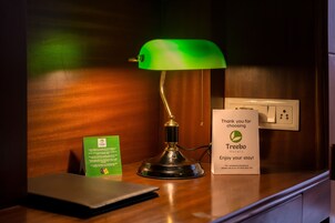 Uma mesa com uma luminária verde, um laptop, uma placa da Treebo Hotels e uma tomada.