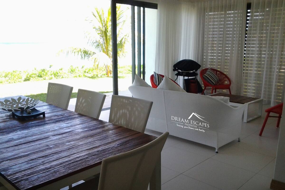 Um hall de hotel moderno com um balcão de recepção de madeira, cadeiras brancas e vista para o exterior.