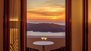 Varanda com uma mesa e duas cadeiras, com vista para o pôr do sol sobre o oceano.