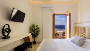 Quarto de hotel com cama, televisão na parede, escrivaninha com cadeiras, planta em vaso e varanda com vista para a paisagem.