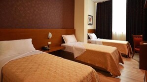 Quarto de hotel com duas camas, cabeceira de madeira, mesa de cabeceira com abajur, um quadro na parede e uma janela com cortinas.