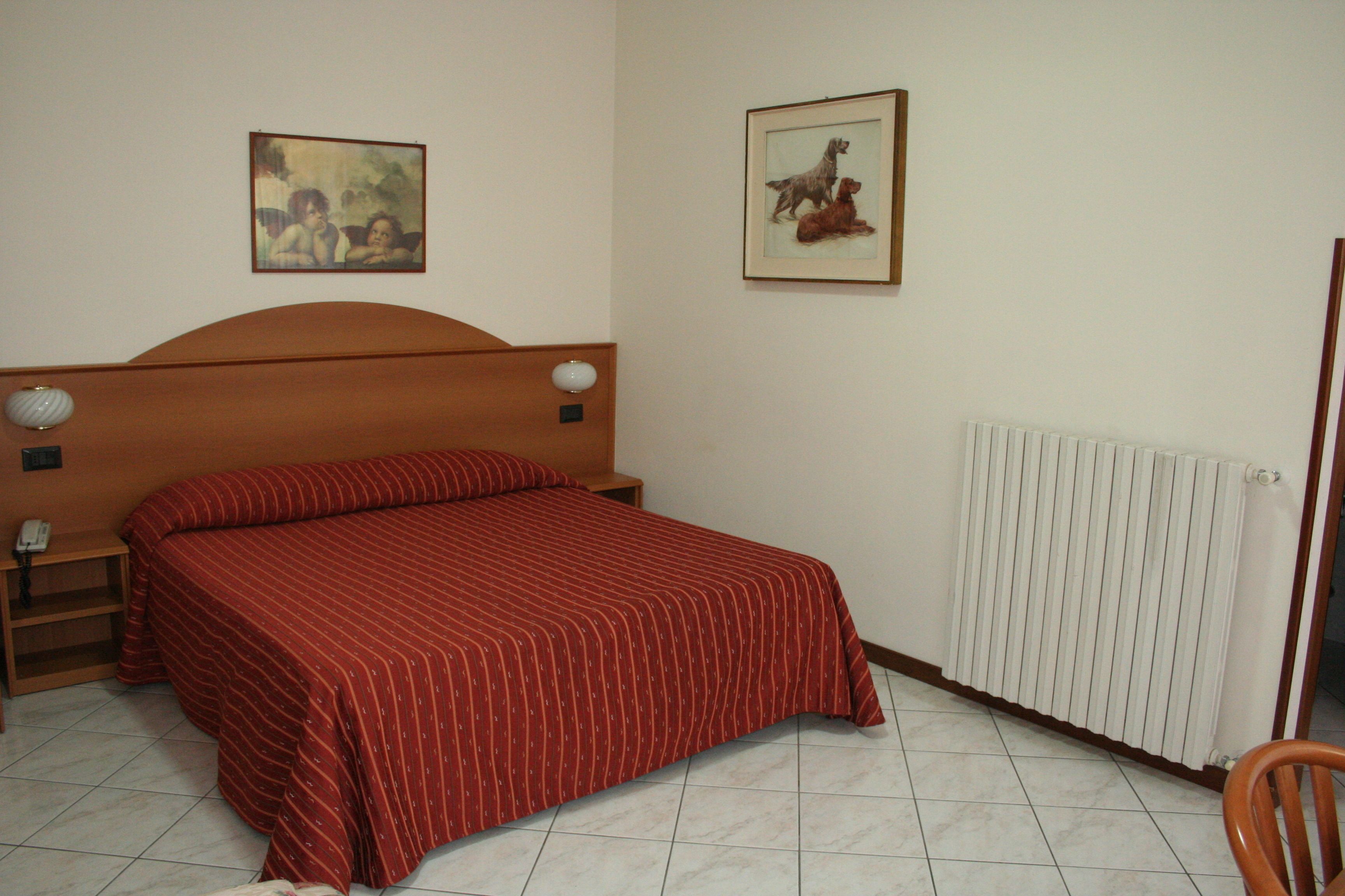 Quarto com cabeceira de madeira, colcha listrada vermelha, radiador branco e duas molduras na parede.