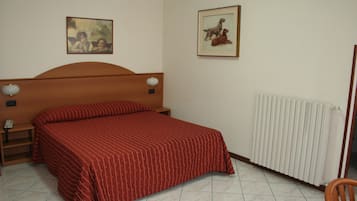 Quarto com cabeceira de madeira, colcha listrada vermelha, radiador branco e duas molduras na parede.
