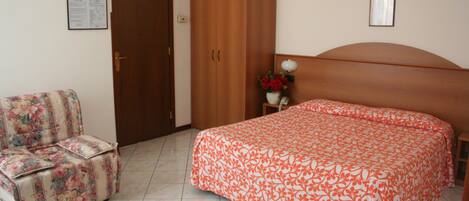 Quarto com uma cama, uma cadeira, um guarda-roupa e uma mesa de cabeceira com um vaso.