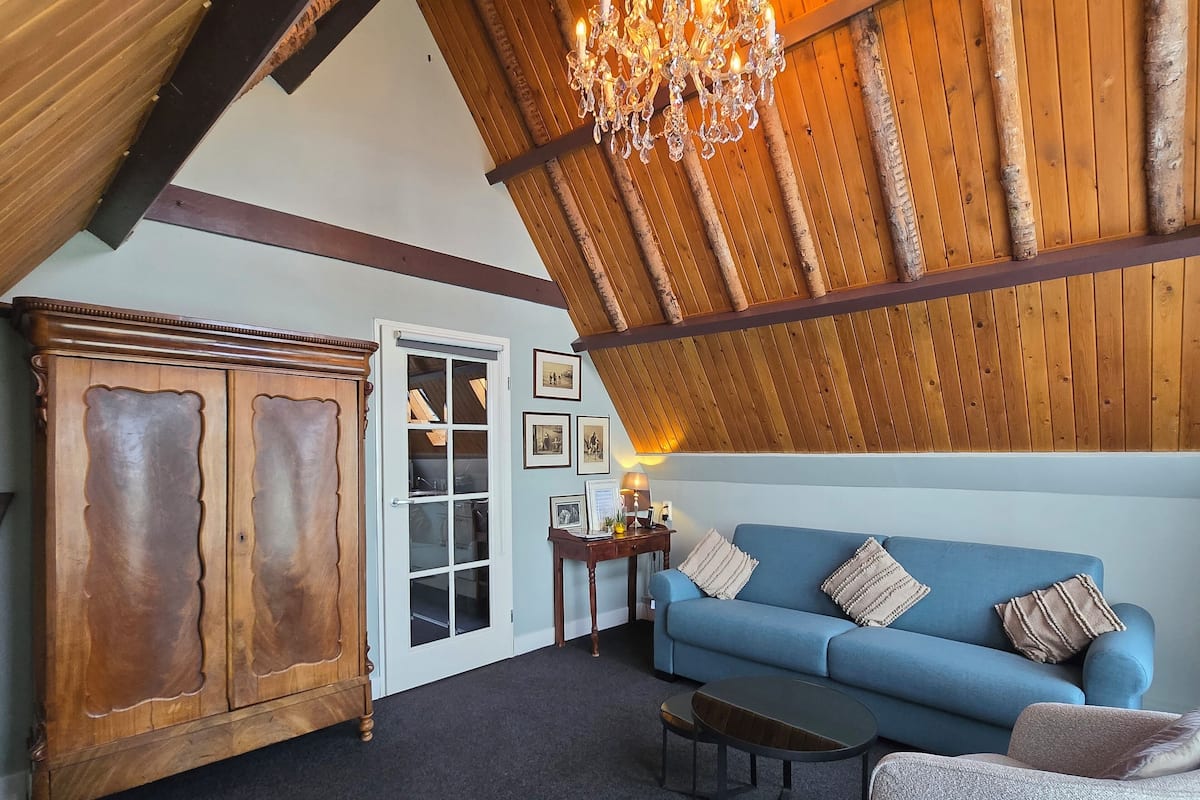 Um quarto aconchegante com um sofá azul, um armário de madeira e um candelabro.