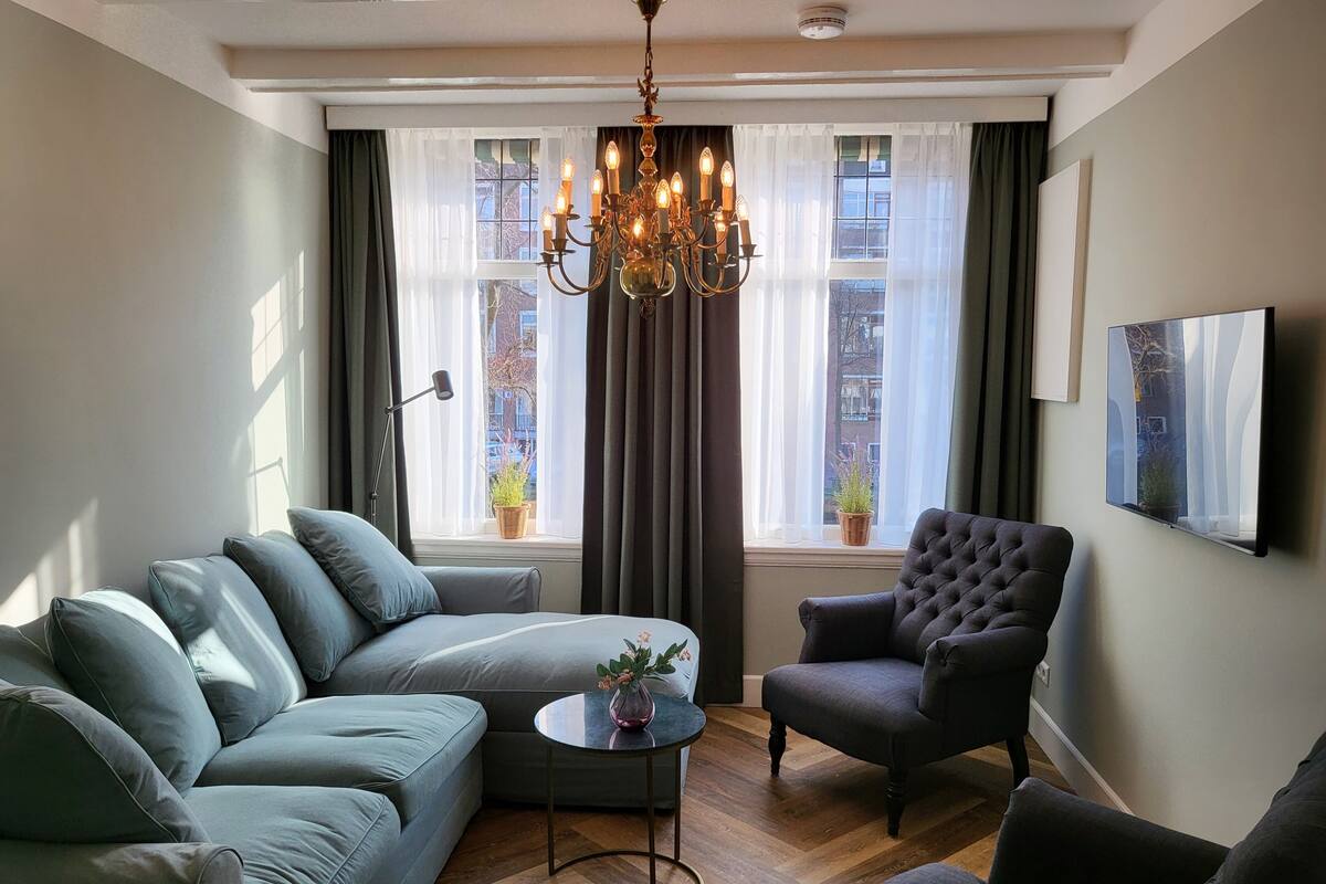 Sala de estar com sofá modular, poltrona estofada, mesa redonda pequena e lustre.