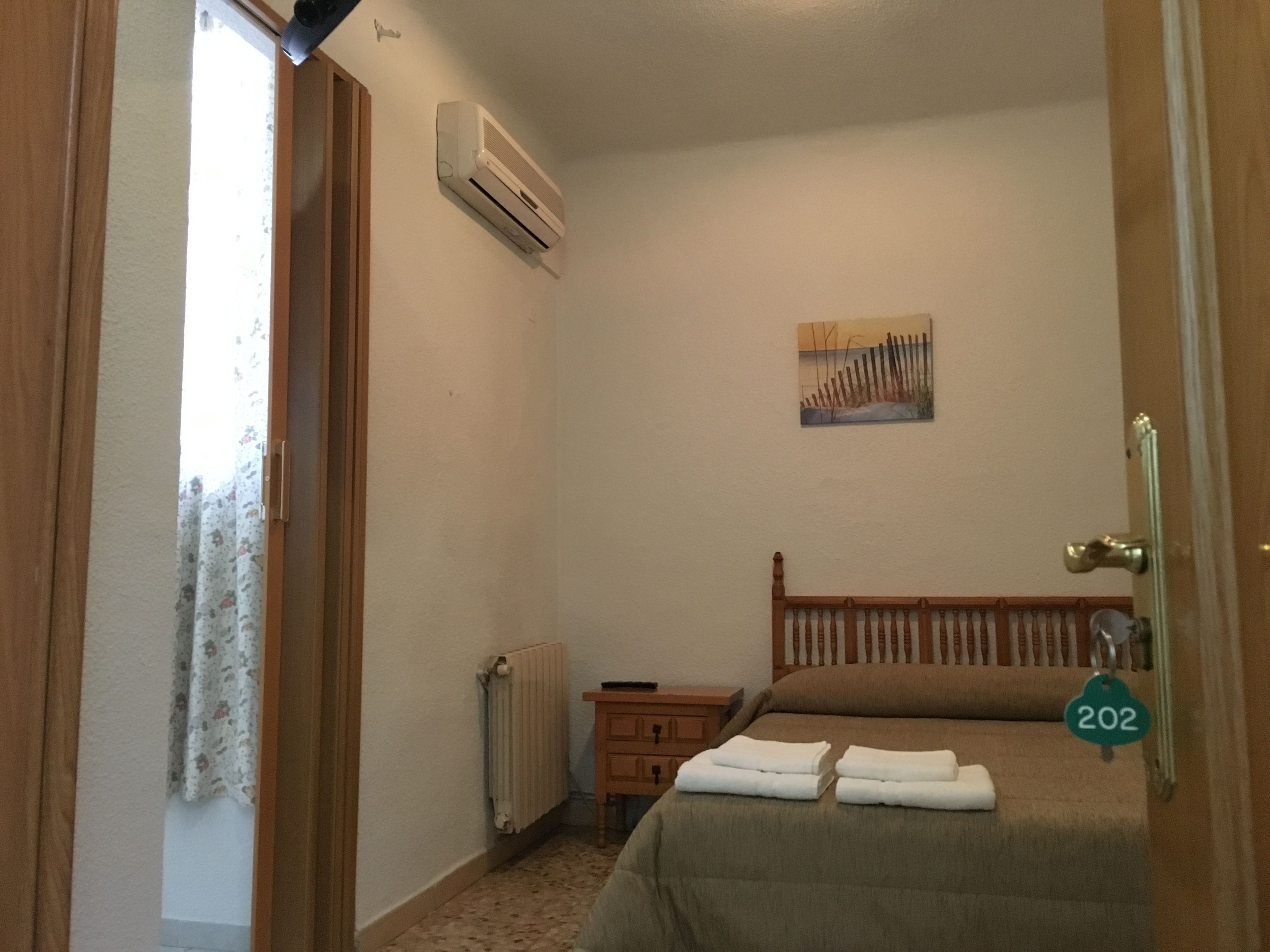 Quarto com cama de madeira, radiador, mesa de cabeceira pequena e ar condicionado fixado na parede.