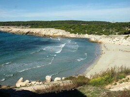 Uma praia costeira com águas cristalinas, linha de costa rochosa e uma área de areia.
