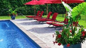 Uma área de piscina com cadeiras de sol vermelhas e guarda-sóis, rodeada por vegetação.