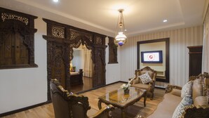 Uma sala de estar tradicional com móveis de madeira elaborados, uma mesa de centro de vidro e uma televisão fixada na parede.