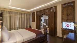 Quarto de hotel com uma cama grande, televisão sobre uma mesa de cabeceira de madeira e um espelho na parede.