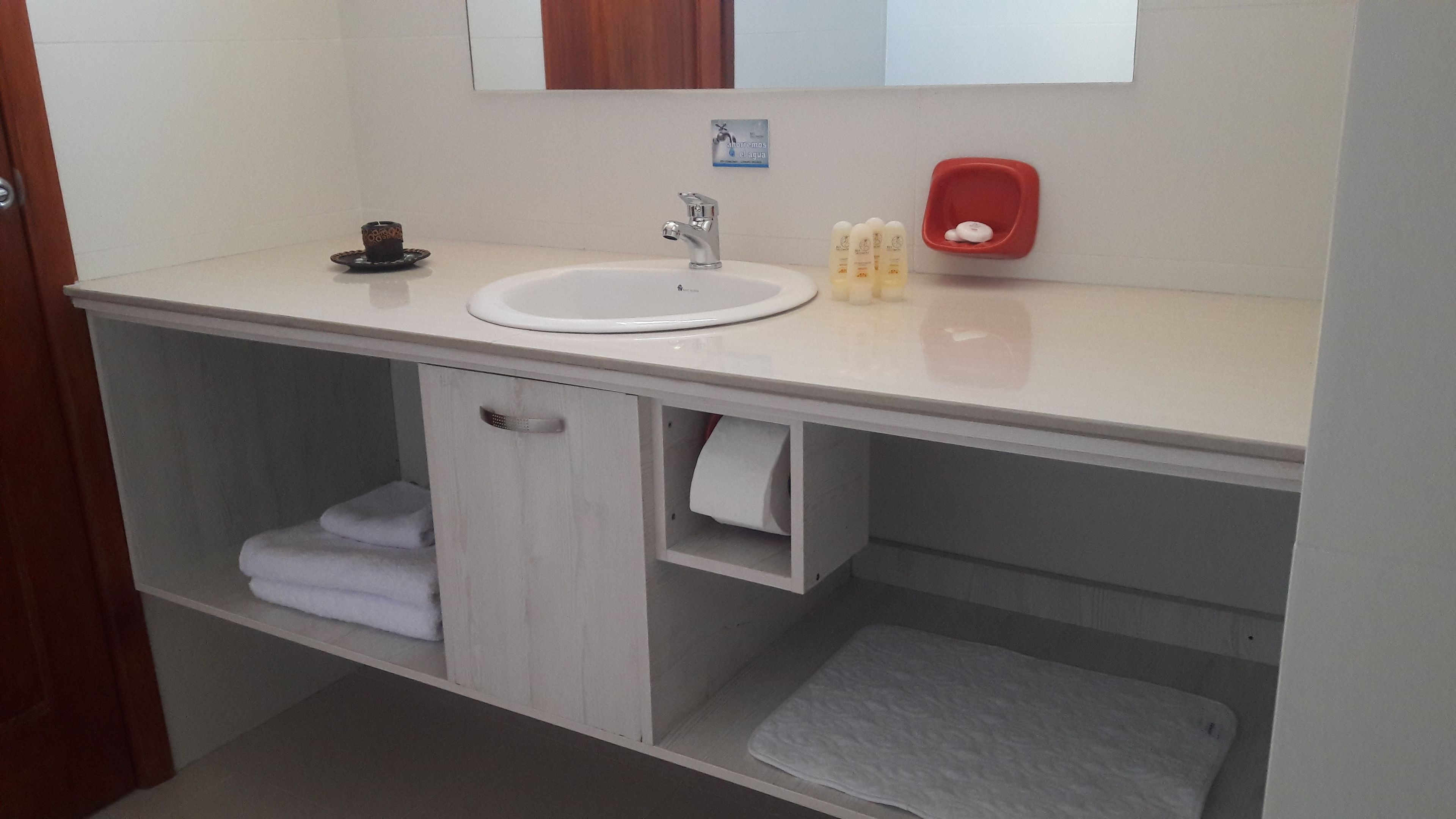 Um banheiro com pia branca, espelho em cima, porta-toalhas e prateleira com produtos de higiene.