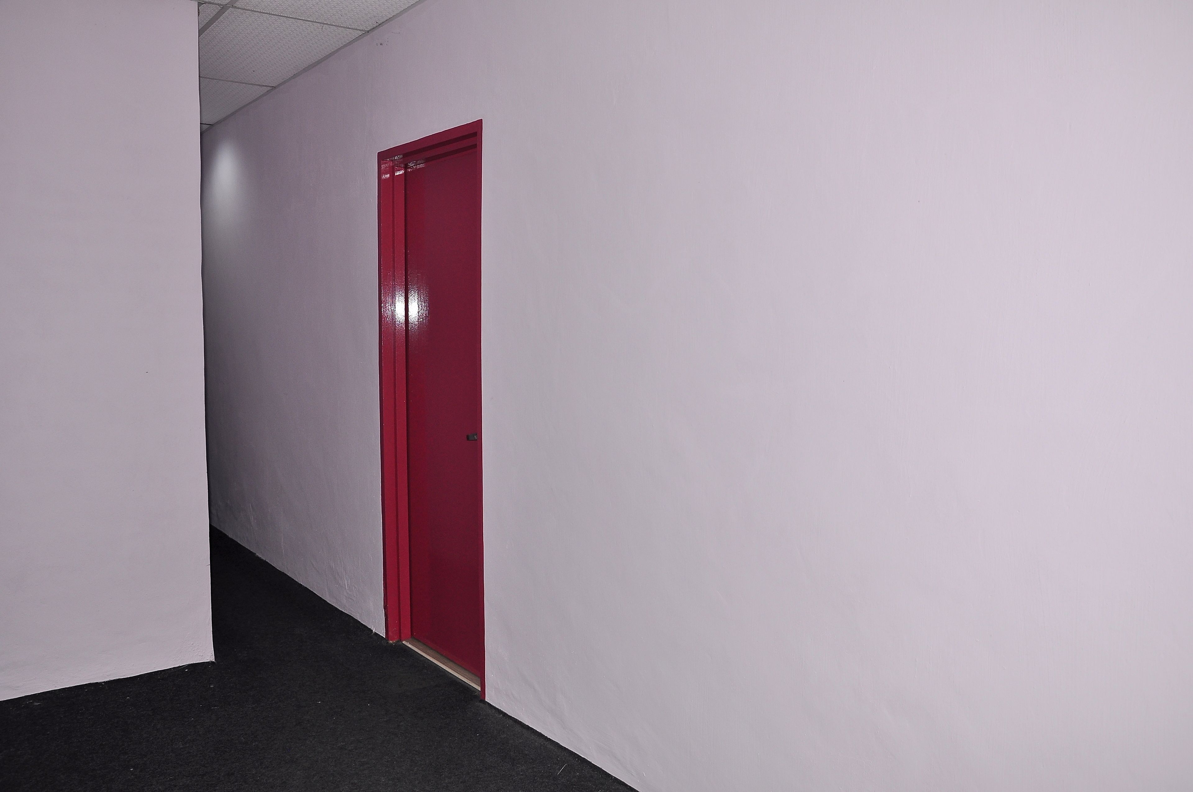 Um corredor estreito com uma porta vermelha no final.