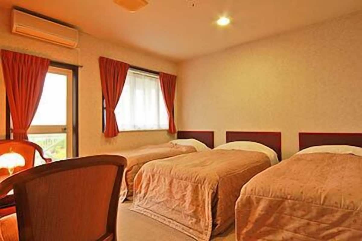 Quarto de hotel com duas camas de solteiro, uma escrivaninha com cadeira e uma janela com cortinas.
