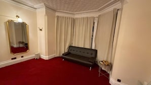 Um quarto com carpete vermelho, sofá preto, espelho grande e uma pequena mesa com uma tigela.
