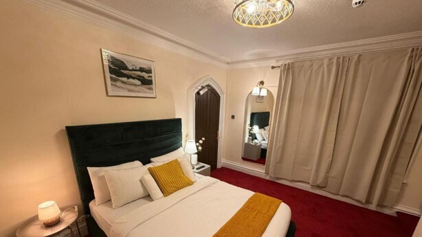 Quarto de hotel com cama, mesa de cabeceira, abajur, espelho e janela com cortinas.