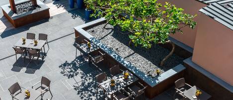 Um pátio externo com várias áreas de estar, lareira e plantas em vasos.