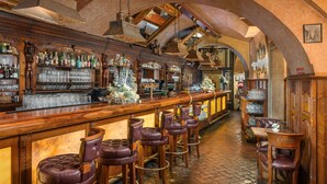 Um bar com banquetas de madeira, chão de tijolos e diversas garrafas e copos em prateleiras.