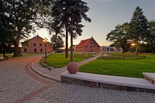 Um pátio com um caminho pavimentado, um banco de pedra e uma grande escultura esférica.