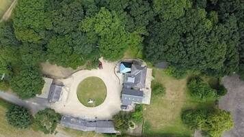 Vista aérea de uma propriedade com um amplo gramado circular, um edifício principal e uma estrutura menor.
