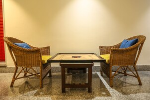 Um quarto com mesa de vidro, duas cadeiras de vime com almofadas e um pequeno banquinho de madeira.