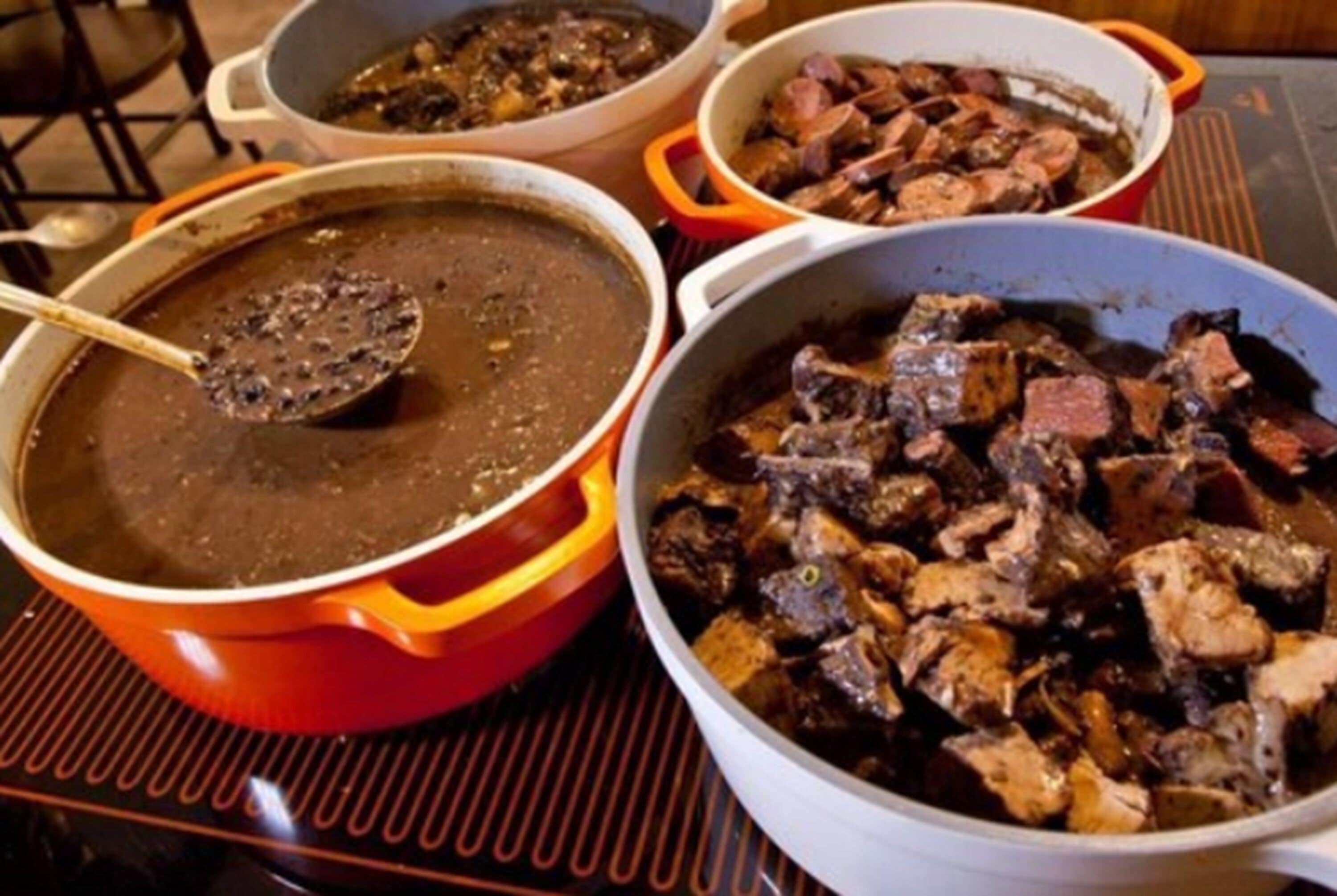 Cozinha com três panelas em um fogão, uma com molho escuro e as outras duas com carne.