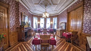 Uma sala de jantar com piso de madeira, toalhas de mesa vermelhas e lustres.
