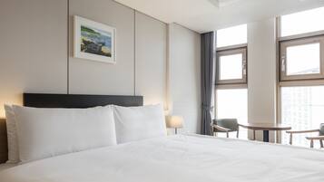 Quarto de hotel com uma cama grande, uma mesa pequena, duas cadeiras, um abajur e um quadro na parede.