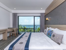 Quarto de hotel com cama grande, escrivaninha e vista para o mar.