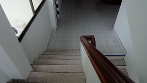 Uma escada com corrimão de madeira leva a um patamar. O chão é revestido com um padrão claro.