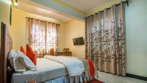 Quarto de hotel com cama, escrivaninha, cadeira e televisão na parede.