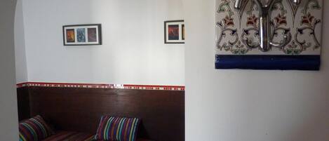 Um quarto com uma cama, duas imagens emolduradas na parede e um azulejo decorativo acima da cama.