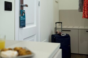 Quarto de hotel com porta branca, interruptor de luz fixado na parede, uma placa com uma mensagem, uma mala e uma mesa com doces.