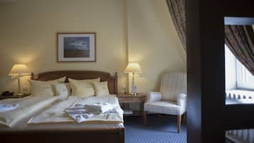 Quarto de hotel com uma cama grande, duas luminárias de cabeceira, uma cadeira, mesa de cabeceira e um quadro na parede.