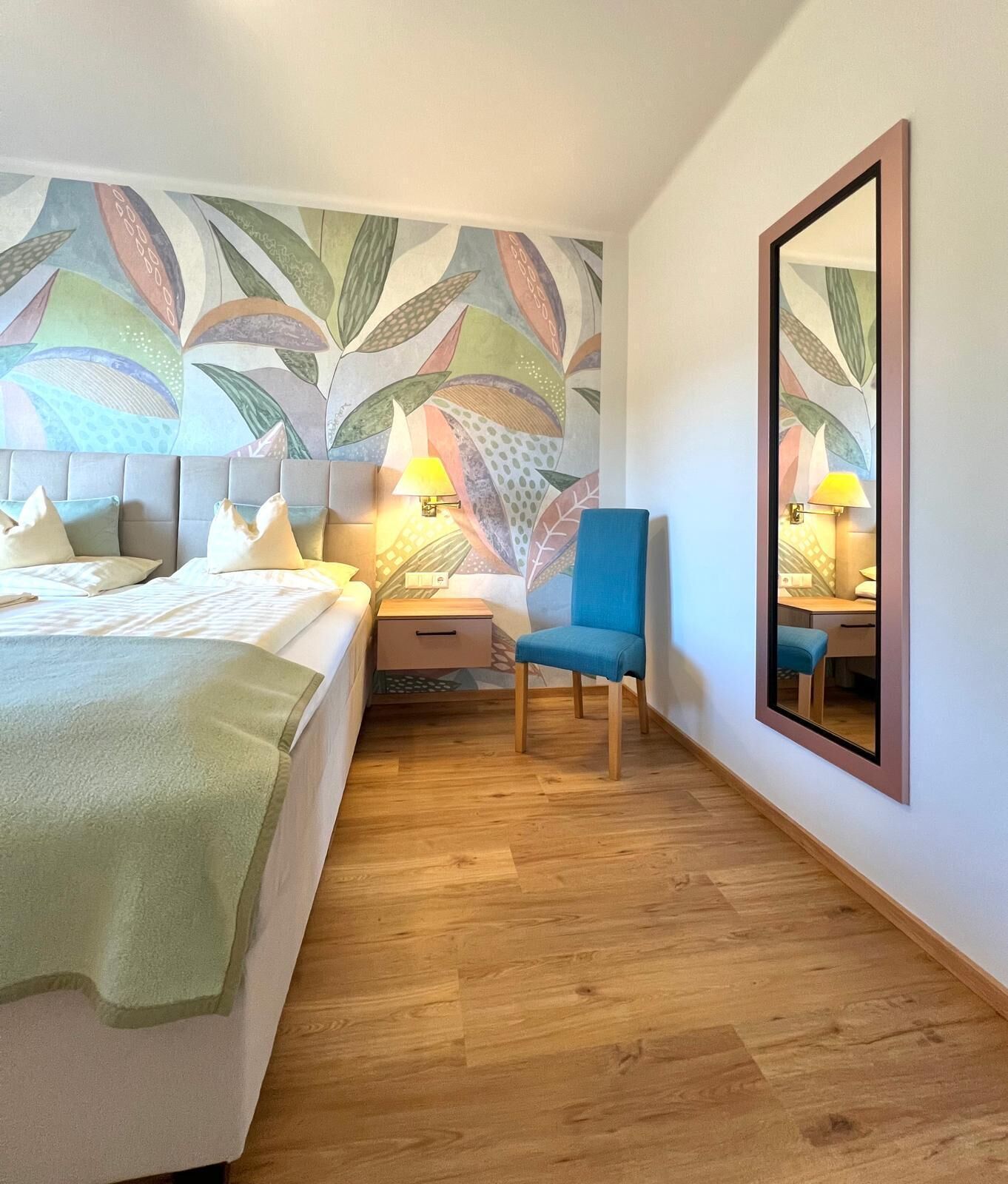 Quarto de hotel com cama, cadeira, escrivaninha e espelho.