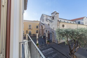 Um pátio com um edifício histórico, uma árvore e um portão.