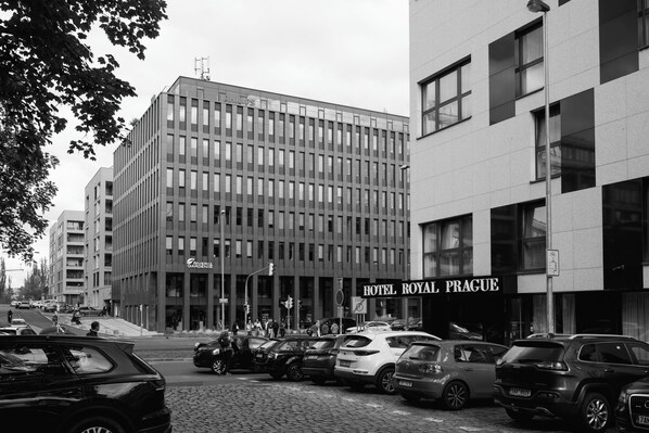 Um edifício com a placa 'Hotel Royal Prague' e uma área de estacionamento com vários carros.