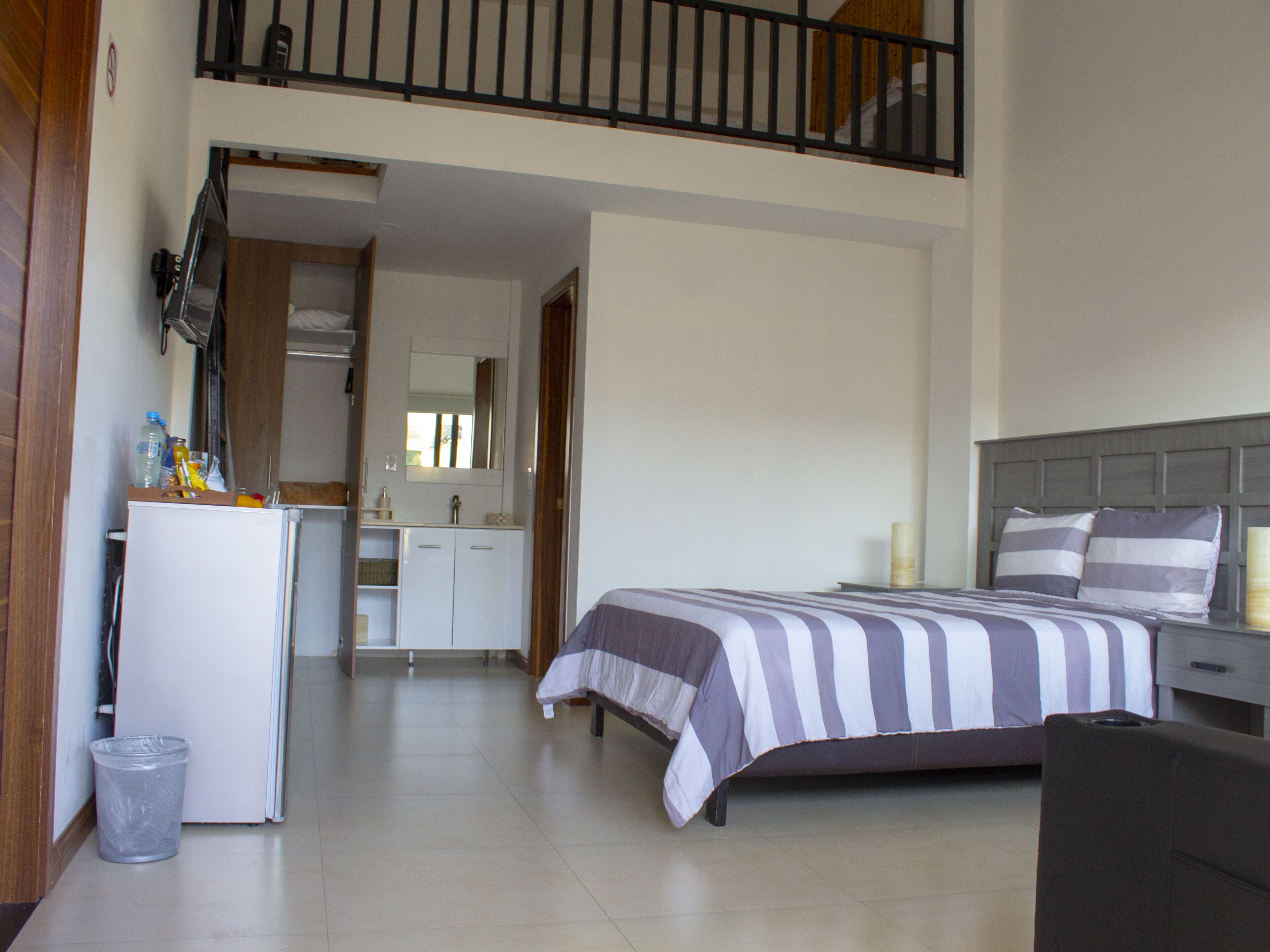 Quarto com cama, escrivaninha, espelho e uma kitchenette.