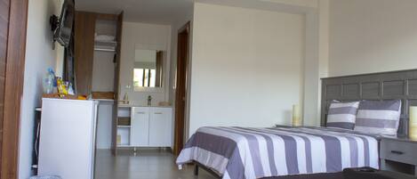 Quarto com cama, escrivaninha, espelho e uma kitchenette.
