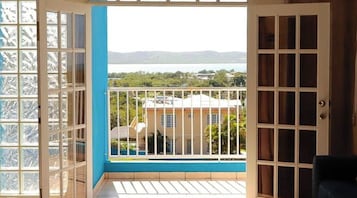 Quarto com varanda e vista para um corpo de água e montanhas ao longe.