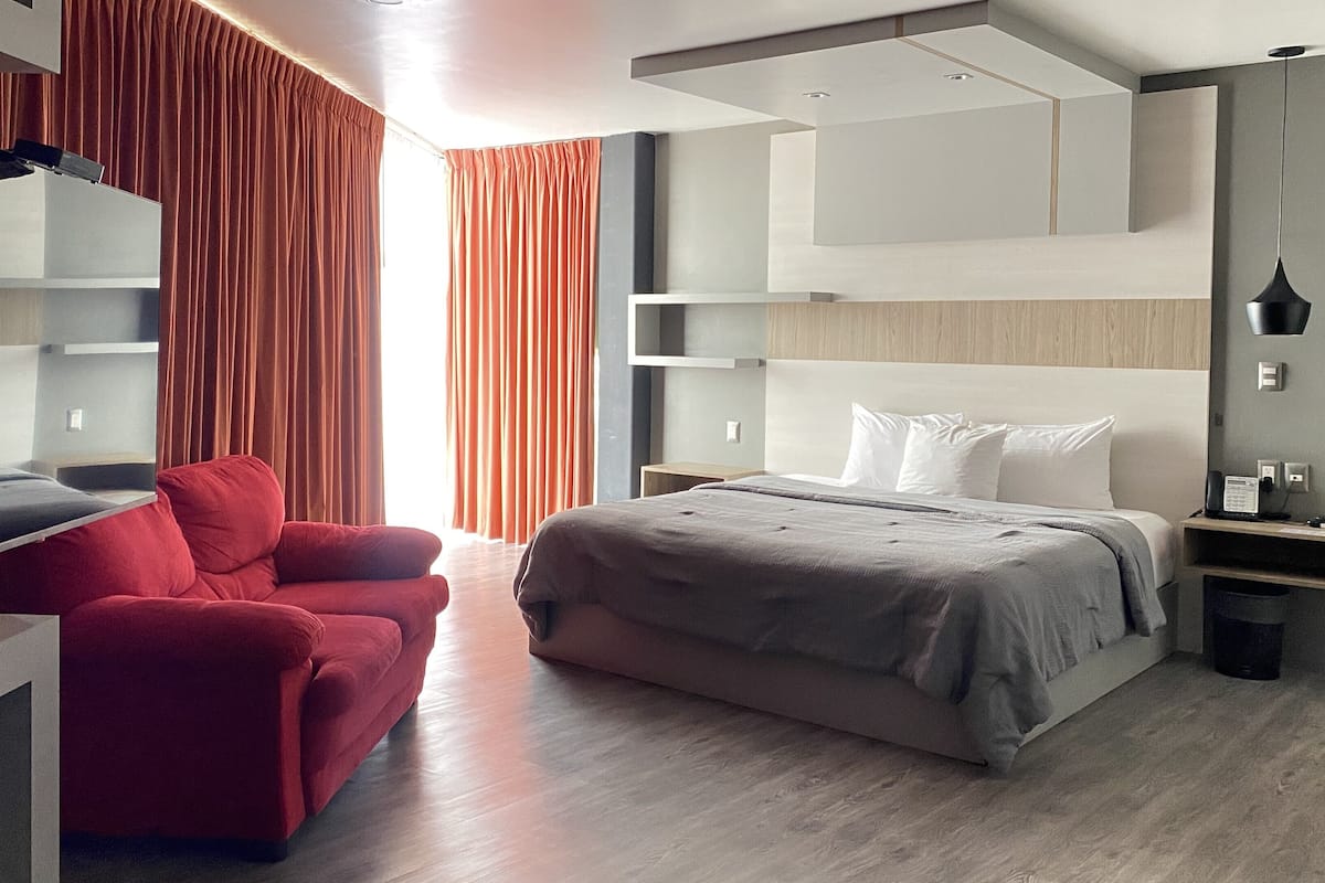 Quarto de hotel moderno com uma cama, uma poltrona vermelha, uma televisão e uma mesa com telefone.