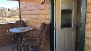 Uma cabana de madeira com uma mesa redonda e duas cadeiras, uma porta com janela, e vista para um cemitério.