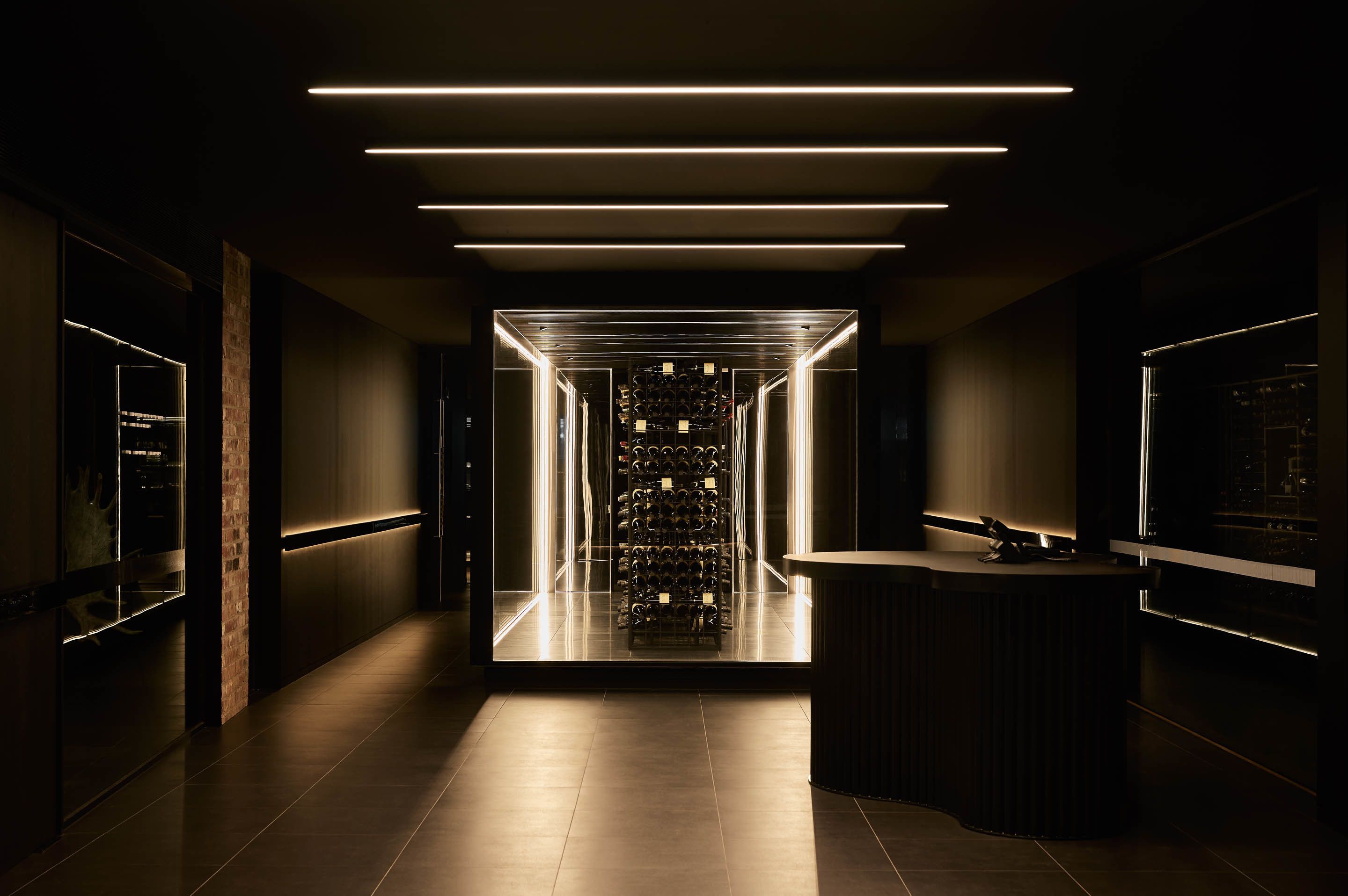 Corredor moderno de hotel com adega, balcão de recepção e iluminação ambiente.